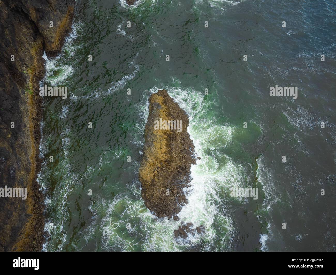 Aerial view. Big boulder in the ocean. White foamy waves wash the stone ...