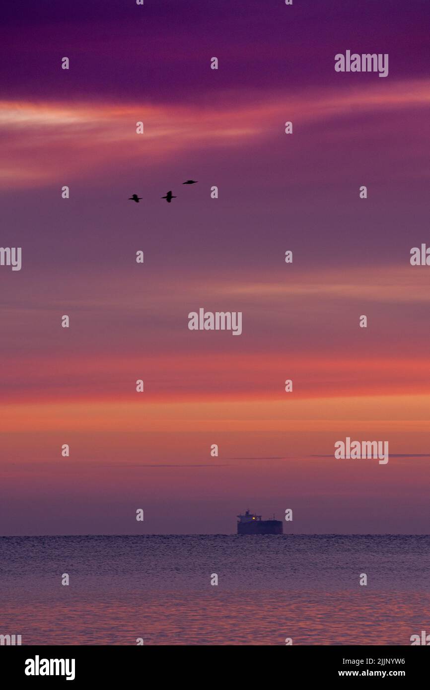 Vertical shot of mesmerizing sunset view with the sea, and silhouettes ...