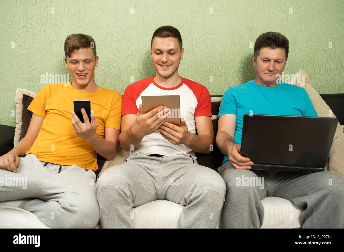 Three young males using different electronic devices while sitting on a ...