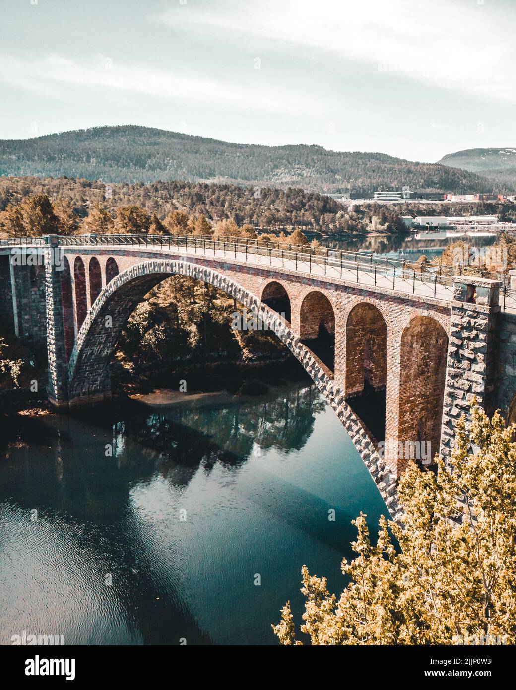 vertical shot of a large stone bridge passing through the big blue ...