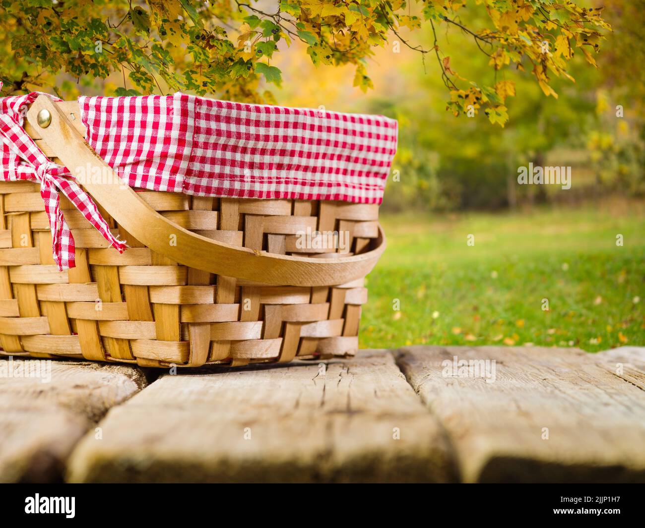 Straw cozy picnic basket on a wooden table against the backdrop of chic ...