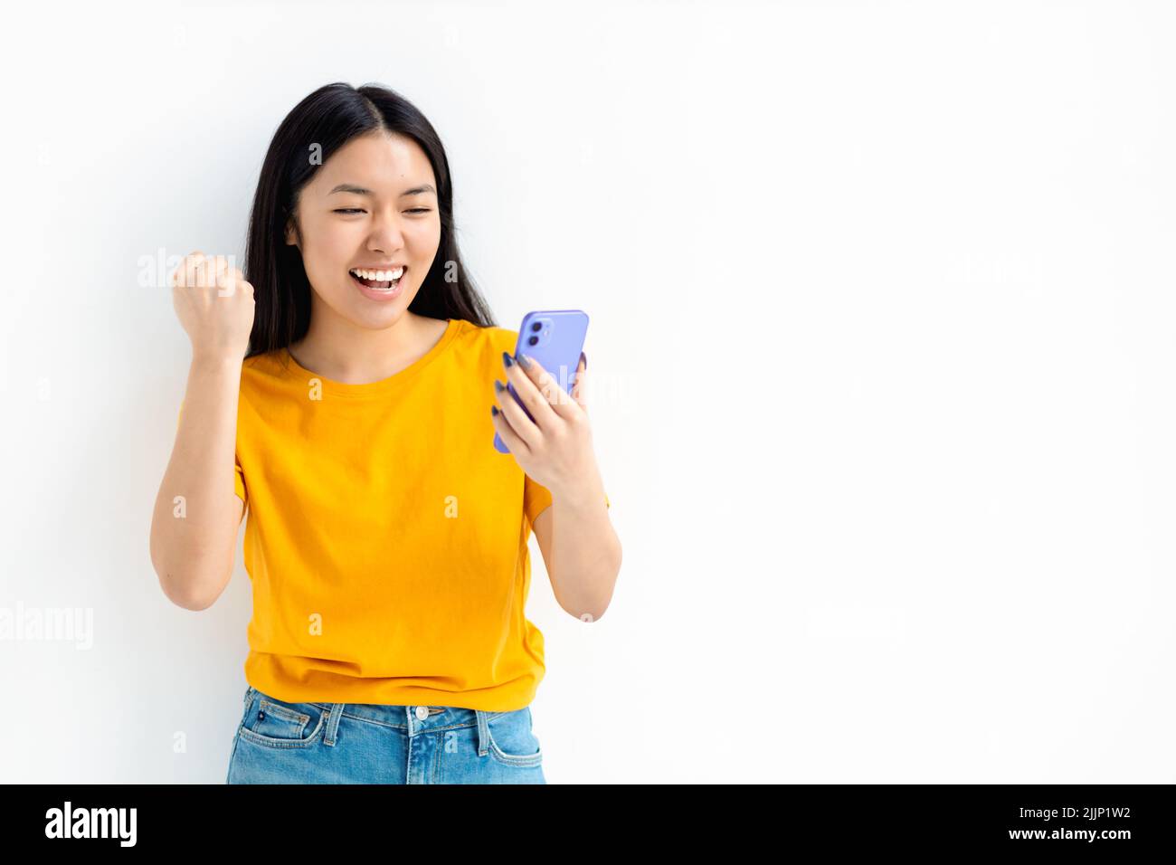 Portrait Of A Joyful Young Asian Woman Holding Mobile Phone And Looking