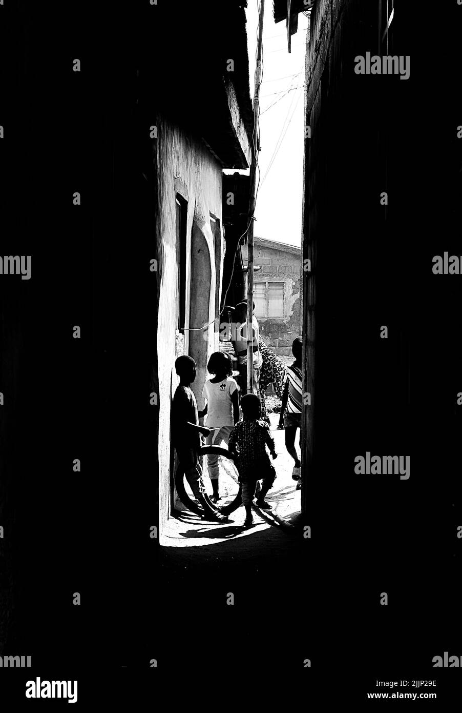 A vertical shot of kids at the end of a narrow dark alley in grayscale ...