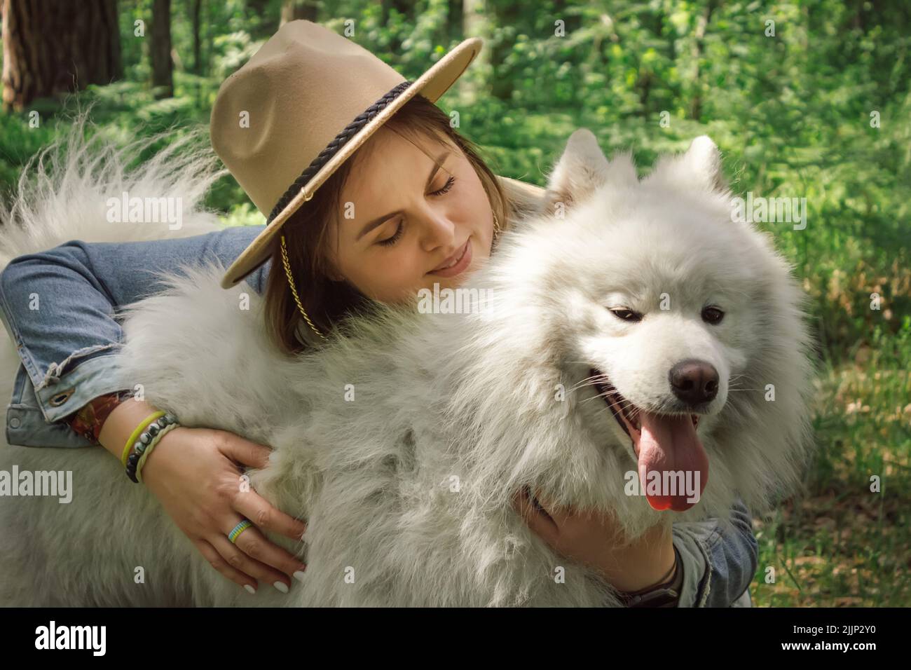 Young beautiful woman hugging her dog samoyed after walking in forest ...
