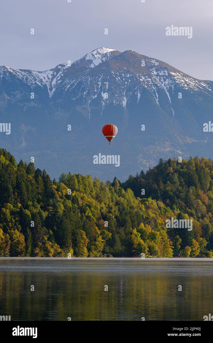 Hot air balloon floating over lake with mountains on the background ...