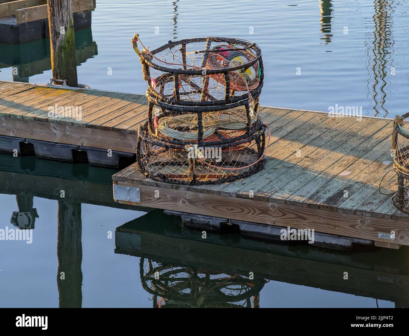A rustic metal round crap trap on wooden dock reflecting on the water ...