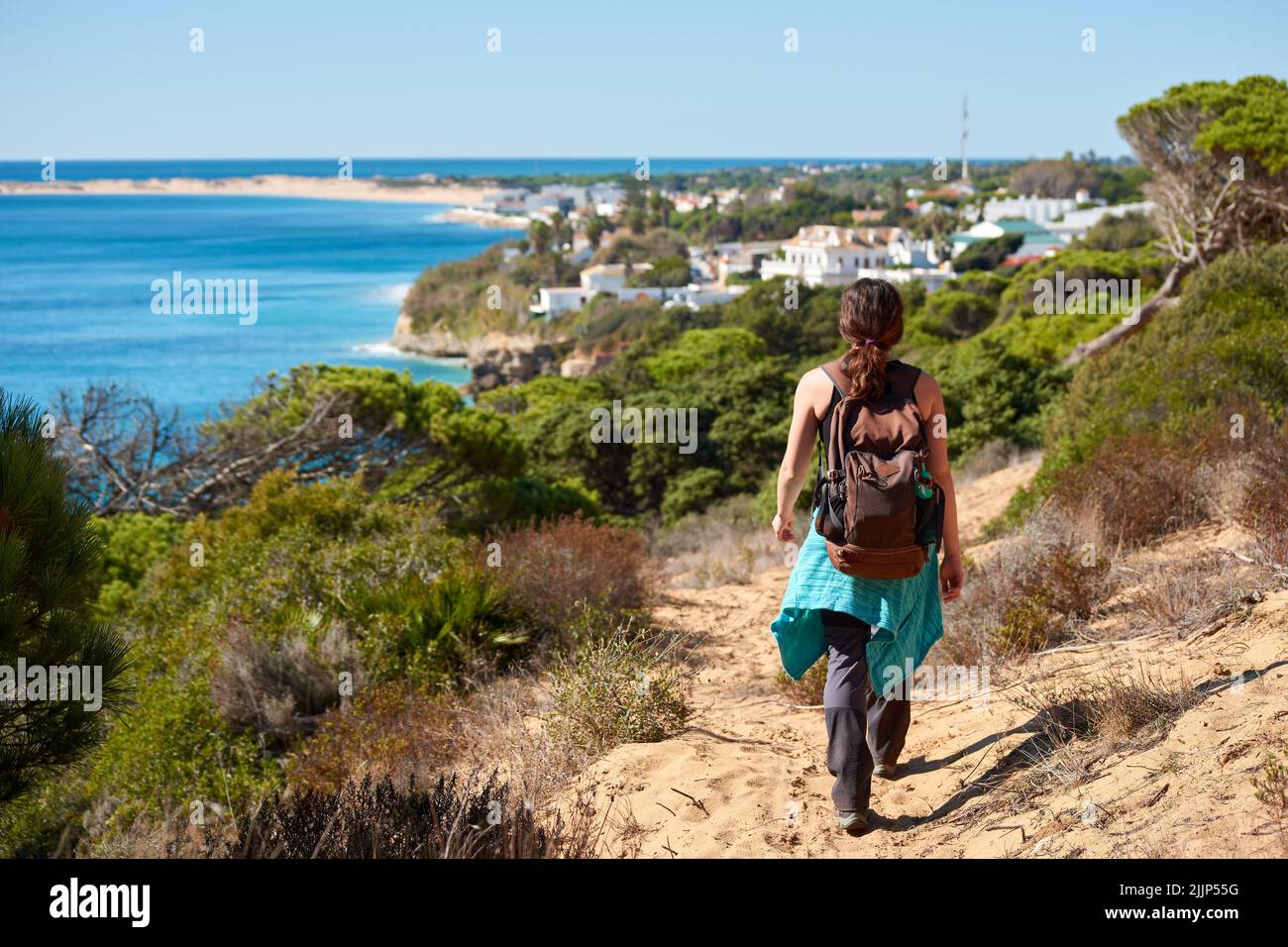A back view of an adventurous female hiker hiking on the sandy hill on ...