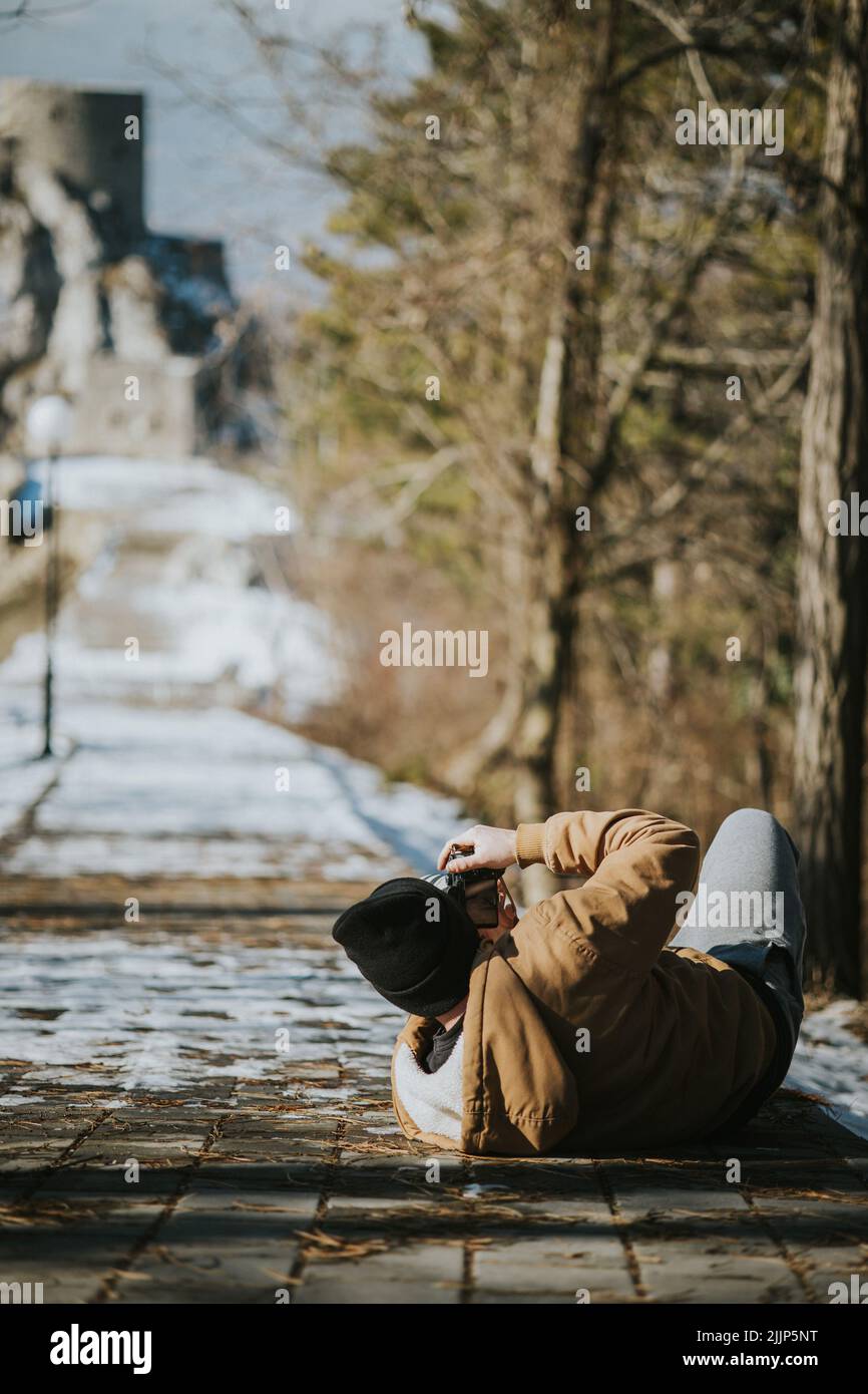 A vertical shot of a man lying on the ground while taking photos with a ...