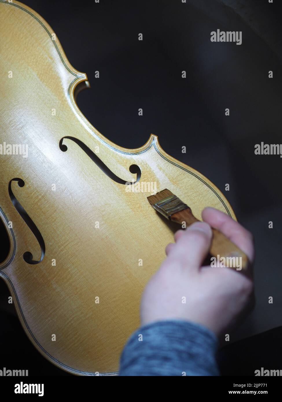 A vertical shot of a luthier painting a violin on the blurry background ...