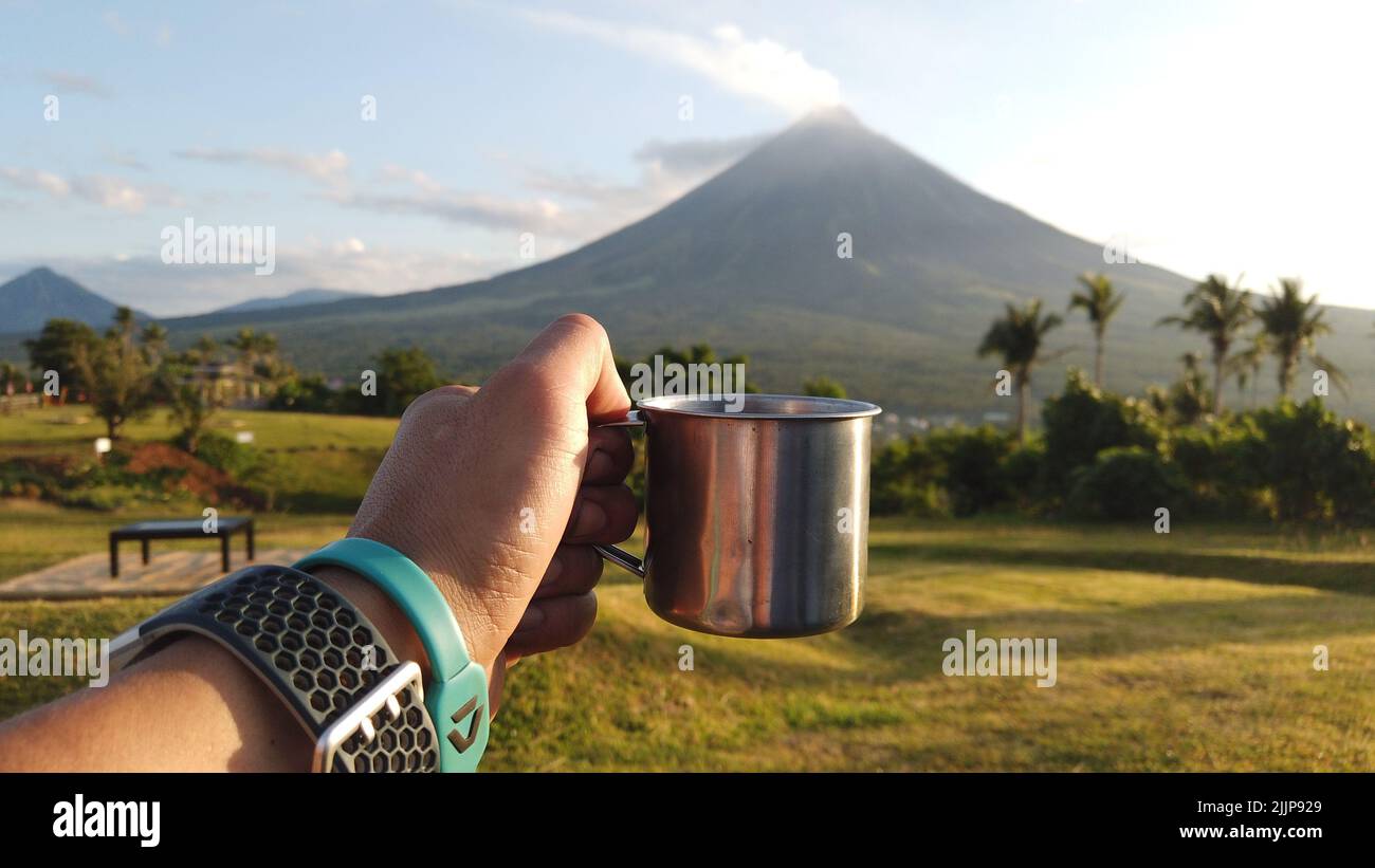 A person's hand holding a metal cup against a beautiful view of the ...