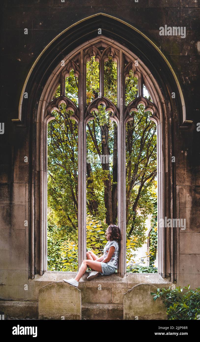 Young woman sitting at the church window at St. Dunstan in the East in ...