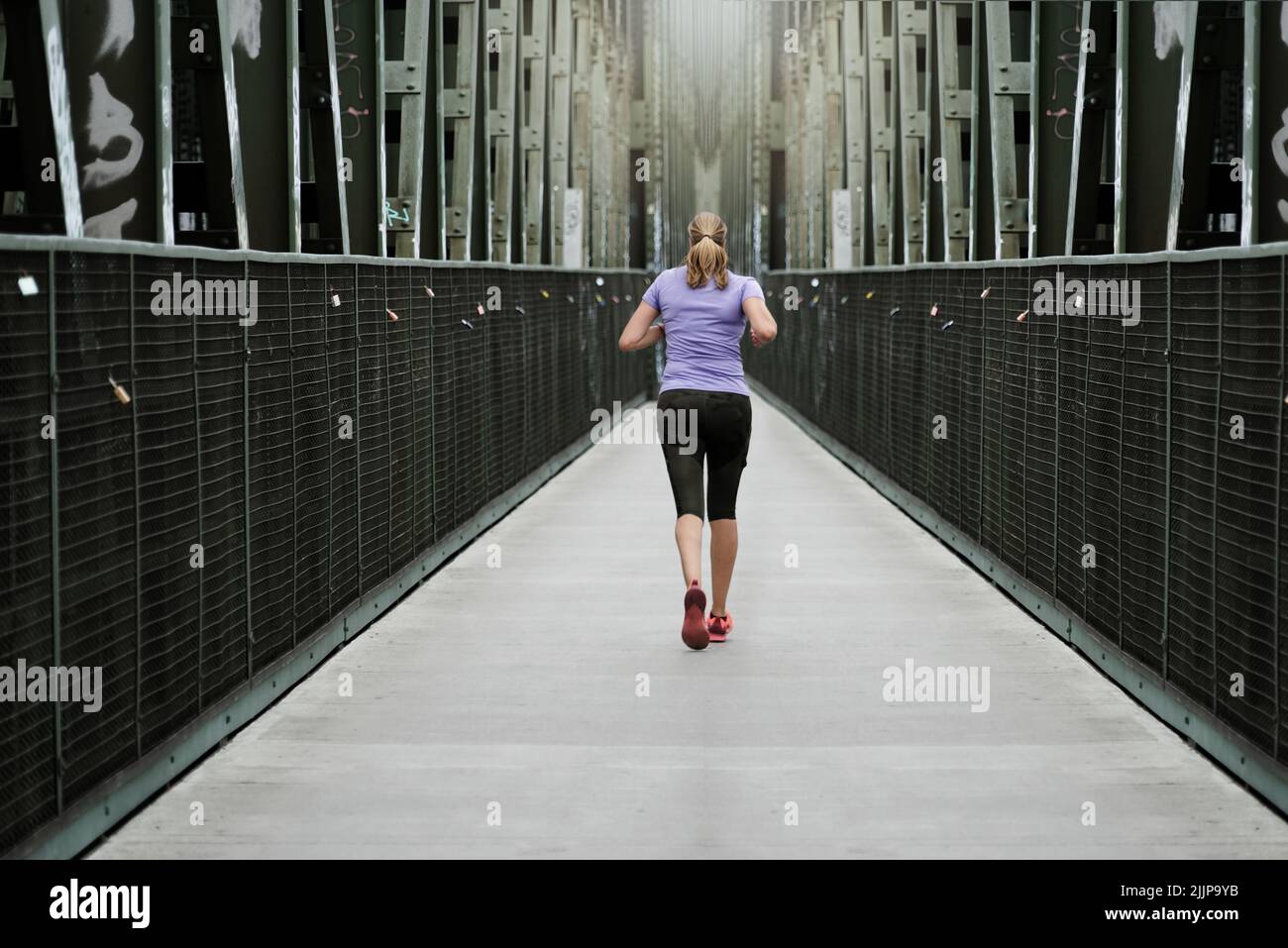 A back view of a woman running down a narrow corridor with metallic ...