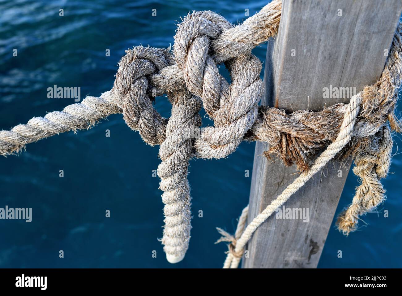 A closeup of a boat rope tied up on a pole on a wooden dock Stock Photo ...