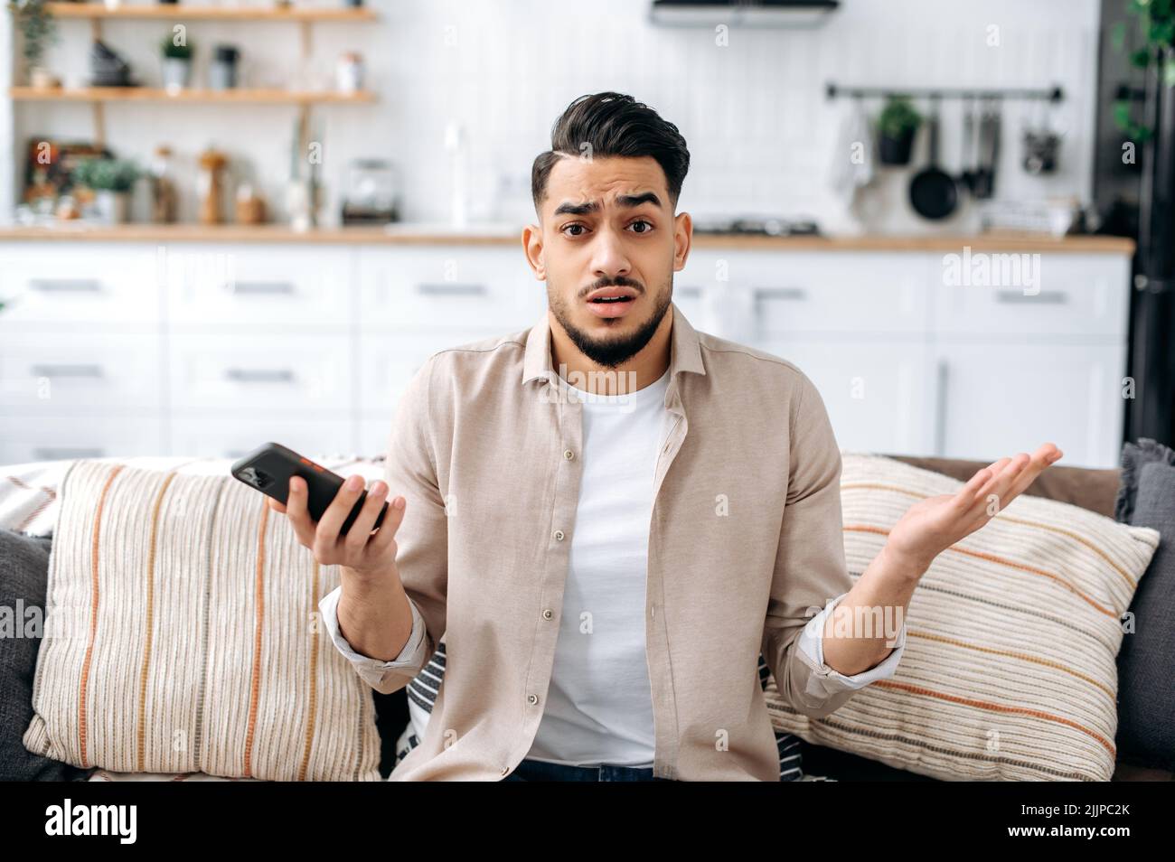 Confused puzzled indian or arabian guy in casual clothes, sits on a ...