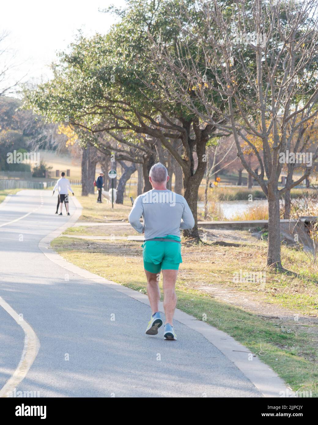 A vertical shot of a male running on sidewalk near White Rock Lake park ...