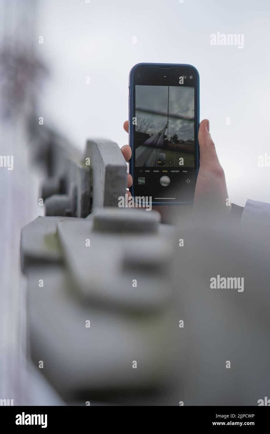 A vertical shot of a hand holding a phone with a camera on a blurred ...