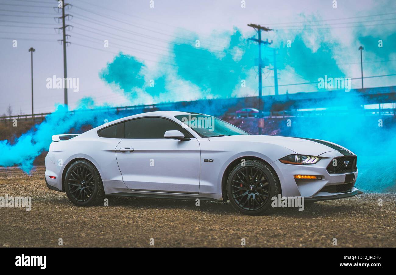 A beautiful shot of a modern white Ford Mustang GT through blue smoke ...