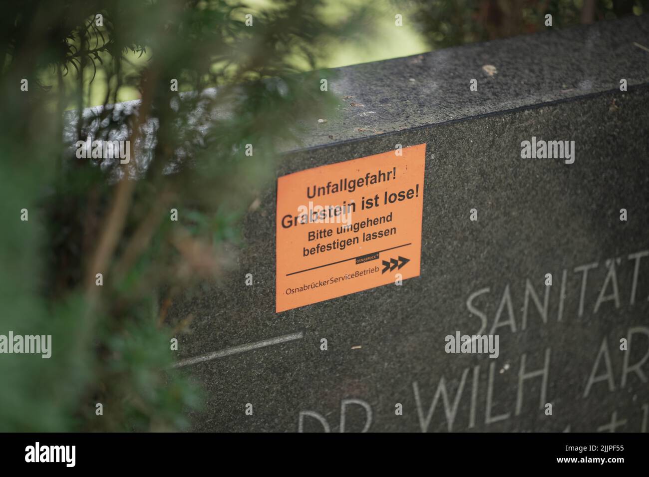 A tombstone with a sticker that says in German: Danger of accidents ...