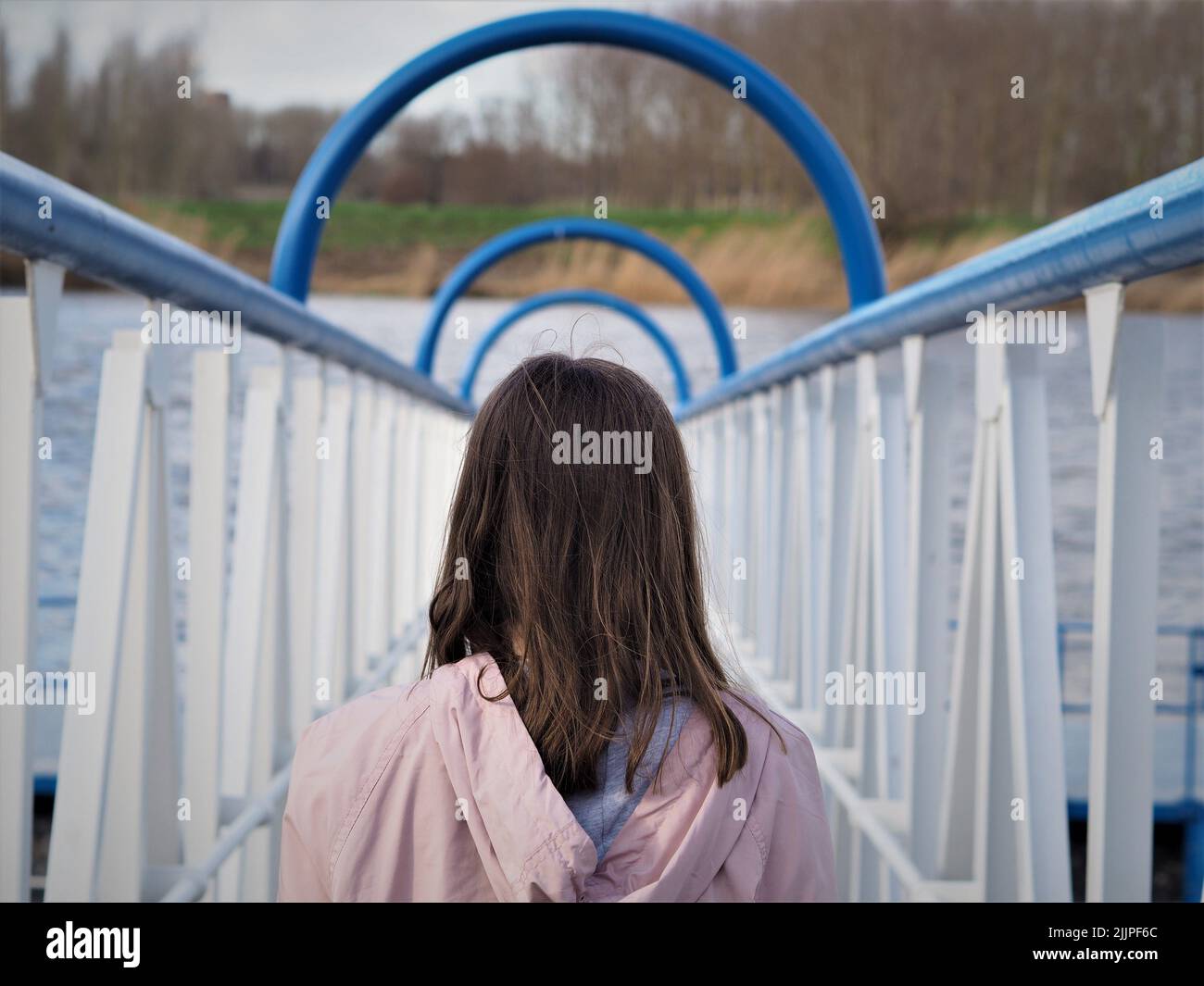 A back view of a young girl standing on a bridge looking at the lake ...