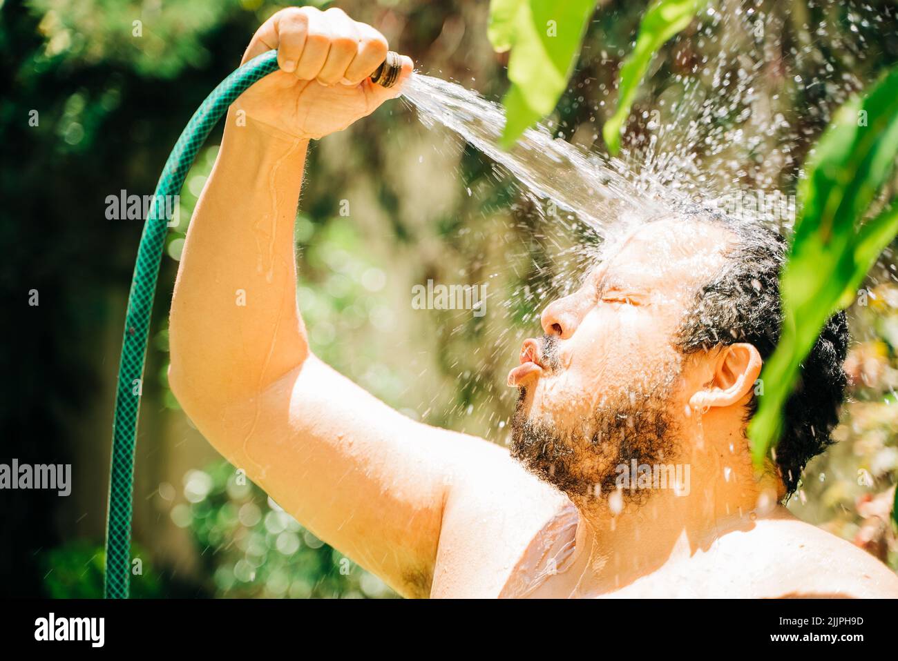 Shirtless man trying to cool himself with water from a hose due to ...