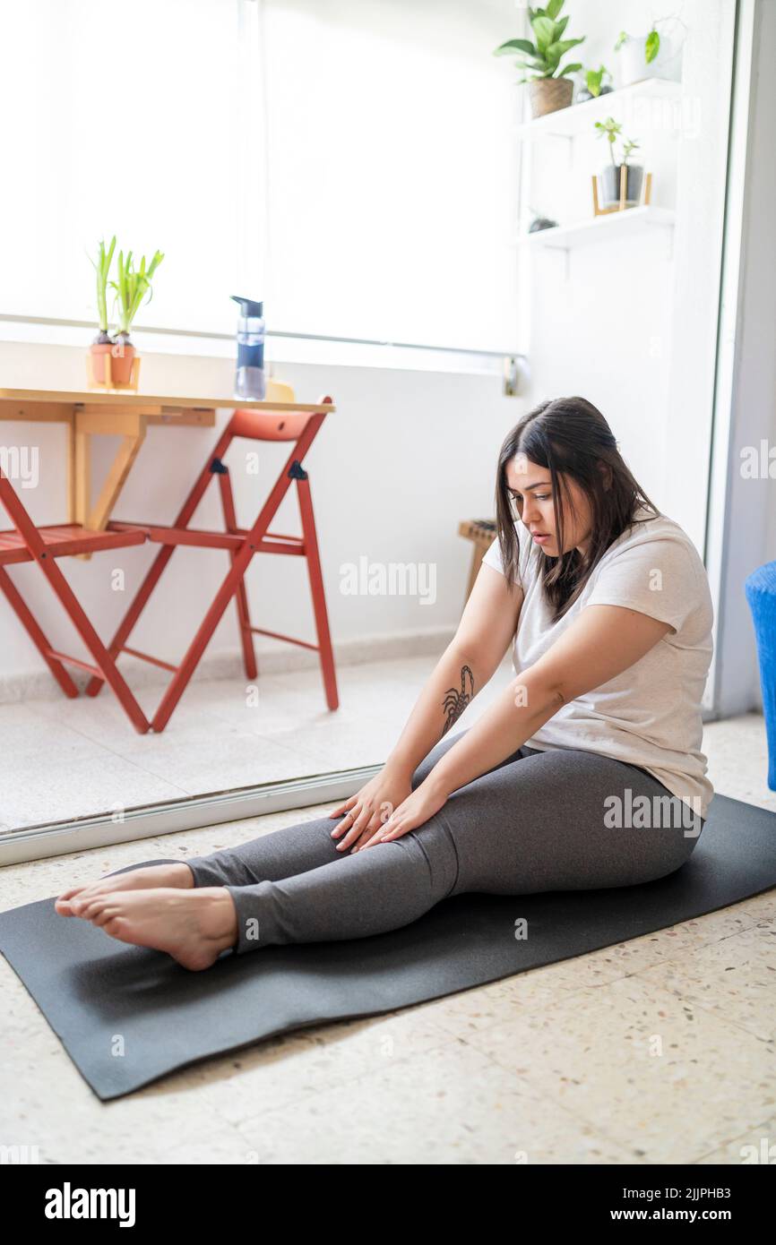 A vertical shot of a young woman showing yoga poses sitting on a grey ...