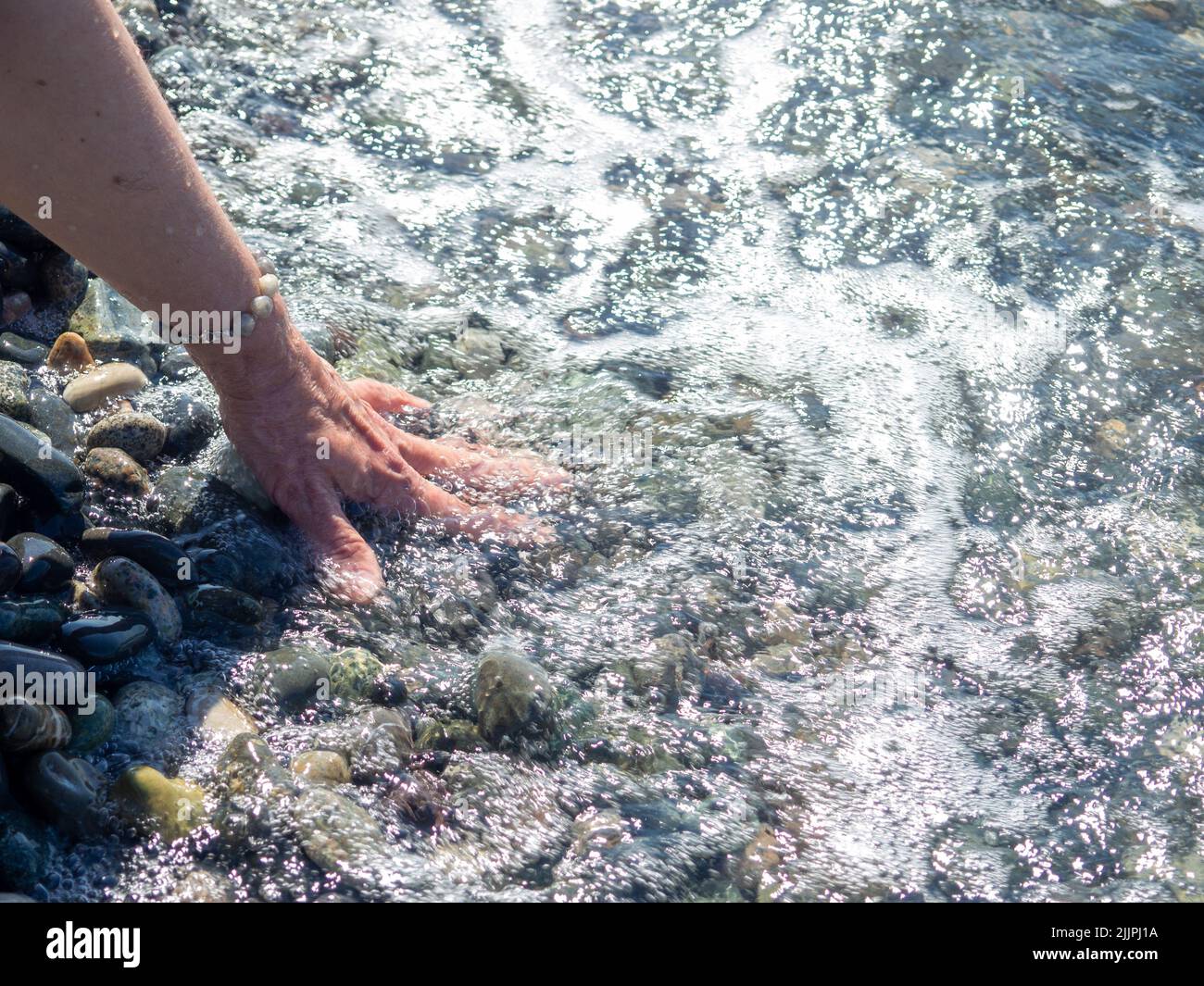 A hand with a bracelet made of stones reaches for the water. Sea wave ...