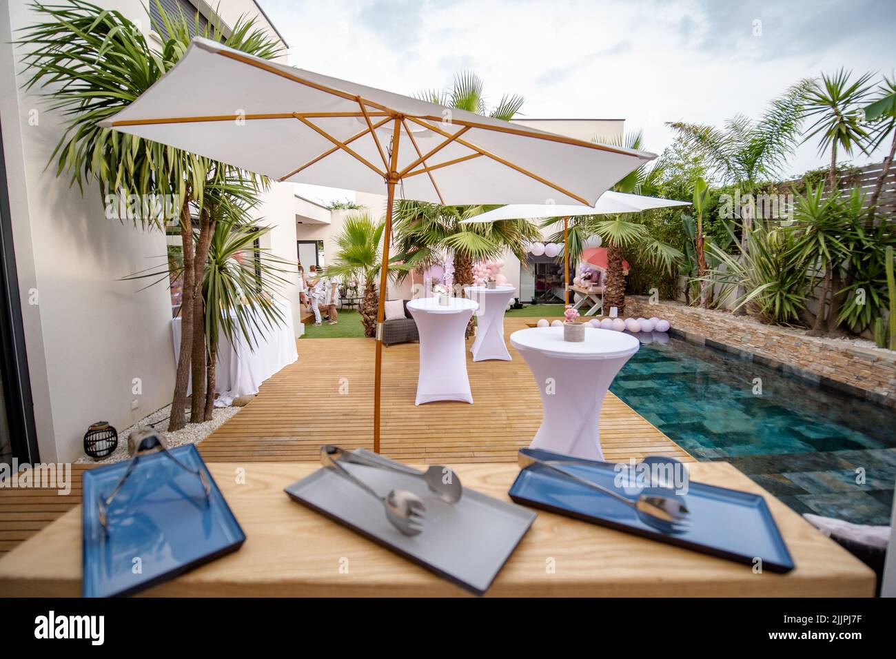 A modern wooden terrace by the pool with high white tables and an empty ...