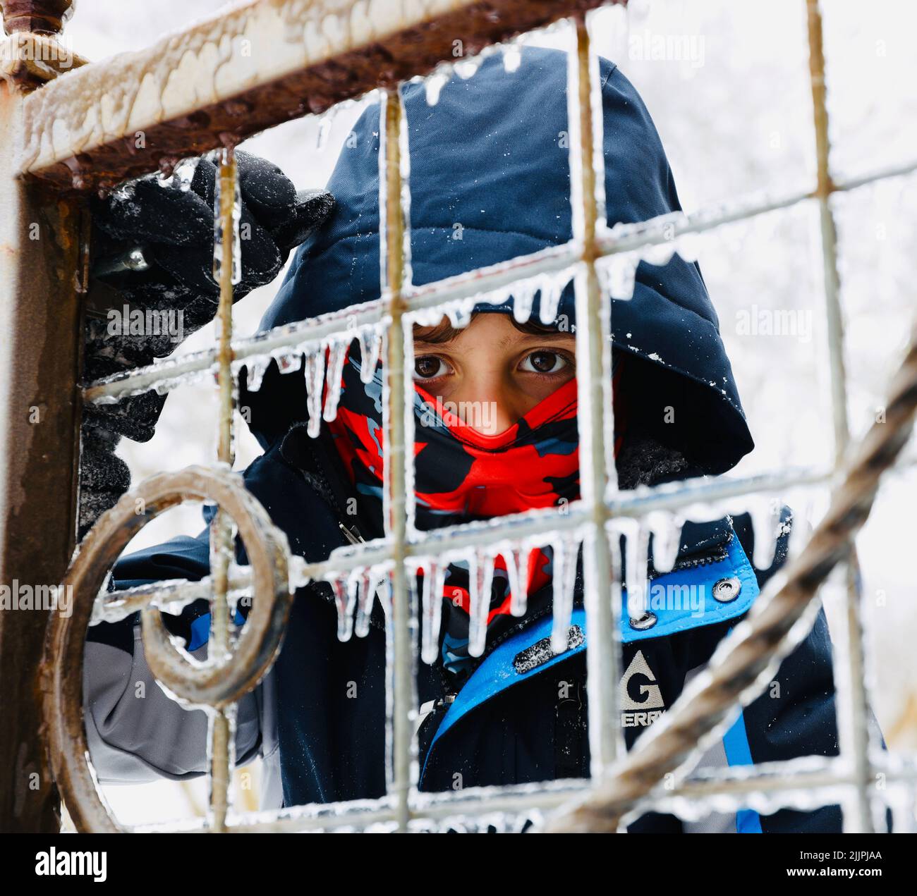 A child wearing a coat and red camouflage face mask, looking through a ...