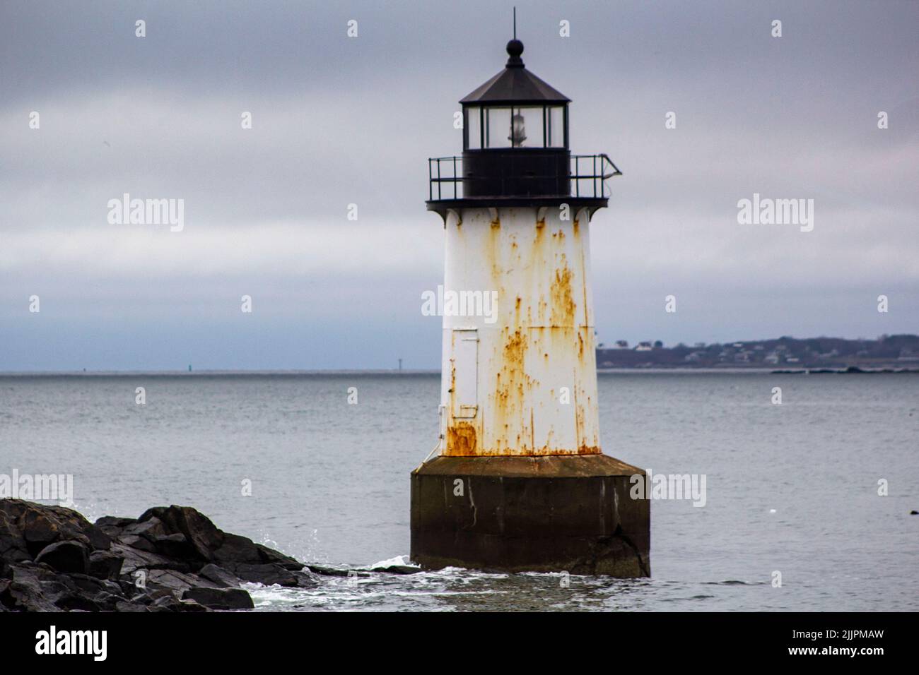 A view of a lighthouse with rusty walls on the sea or ocean shore in ...