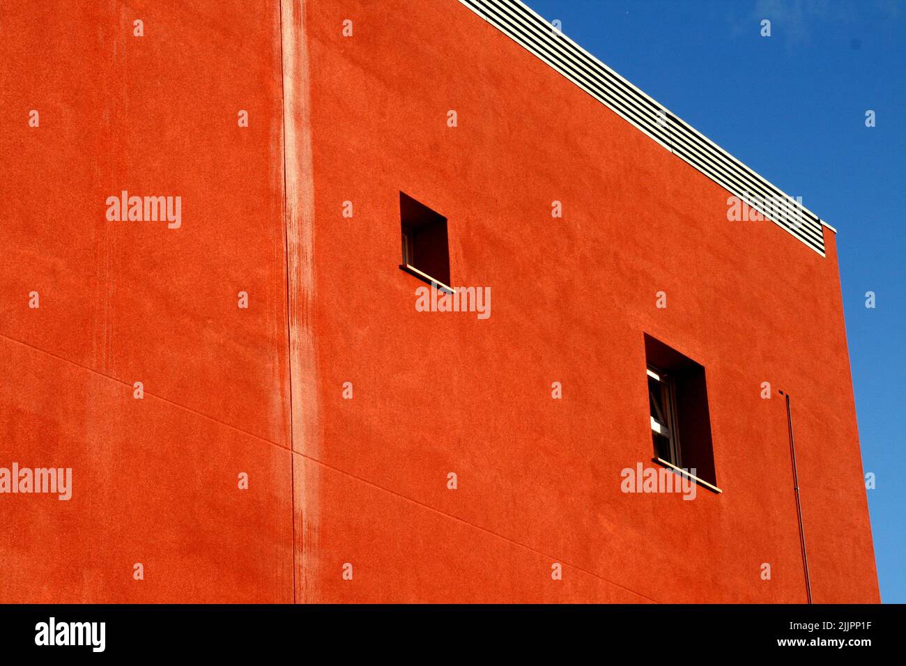 A red wall of the building with two windows on the clear sky background ...