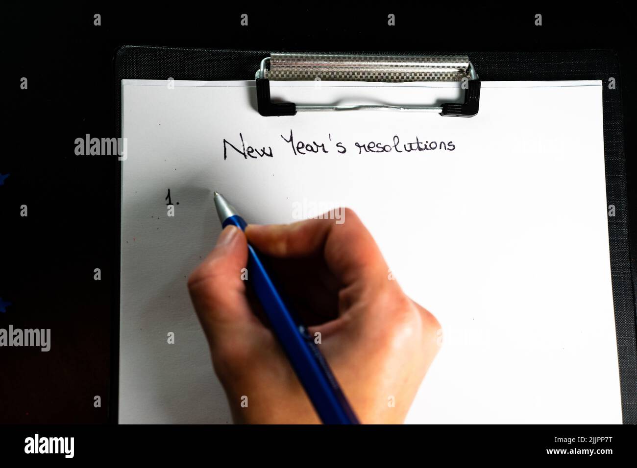 A person holding a pen writing a New Year's resolution on white paper ...