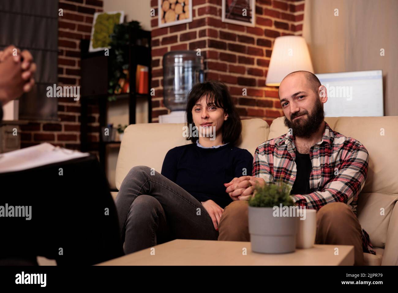 Happy man and woman holding hands after solving problems at therapy session with male therapist ...