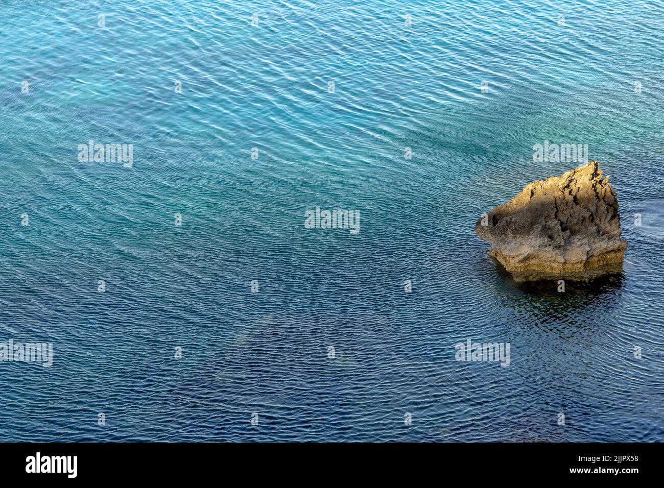 A piece of rock in shallow blue clear water Stock Photo - Alamy