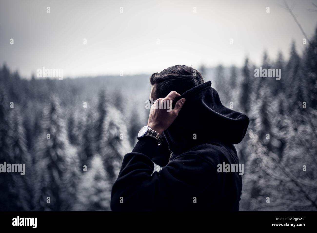 A man with a wrist watch putting on the hood of his jacket with a snowy ...