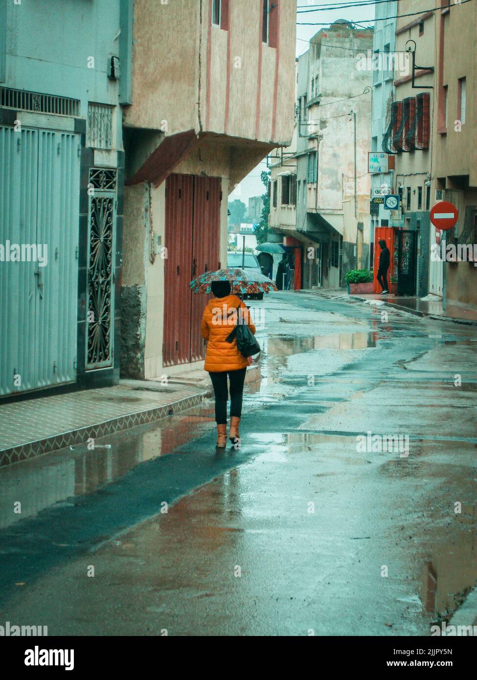 A female with a yellow jacket and umbrella walking in empty street on a ...