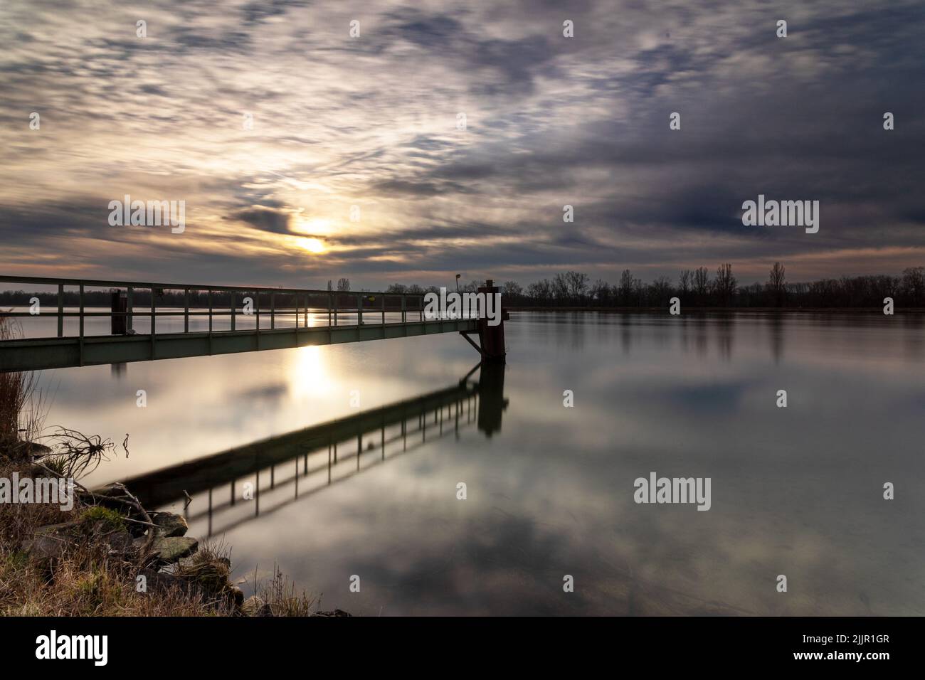 A wooden pier and its reflection in the lake on cloudy sunset sky ...