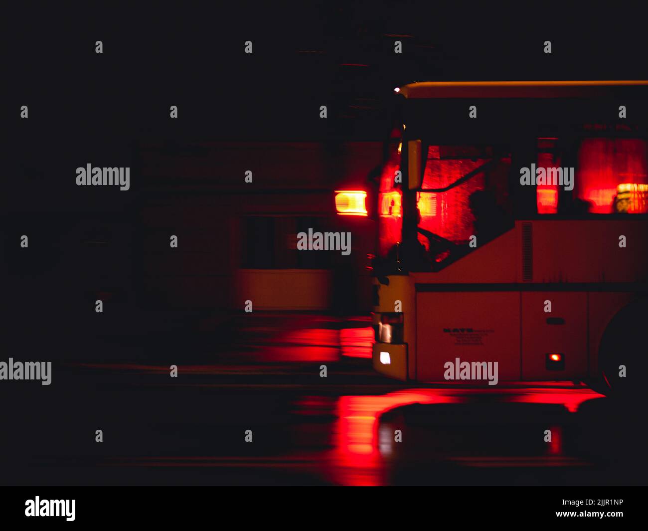 A long exposure shot of the part of a big bus at night with red lights ...