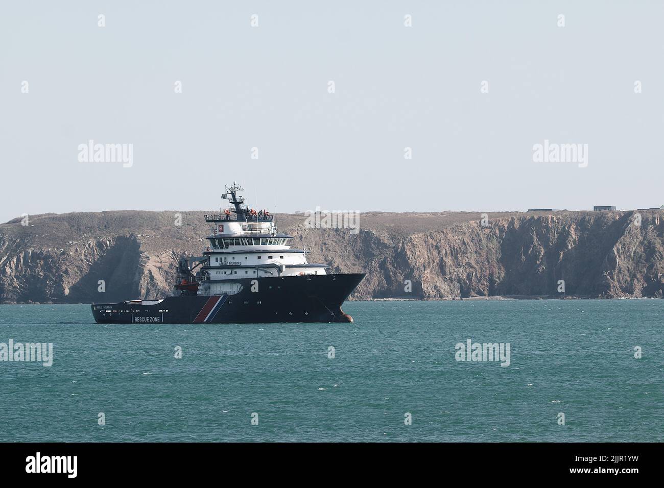 A cargo ship at sea near a steep cliff on a sunny day. A picture ...