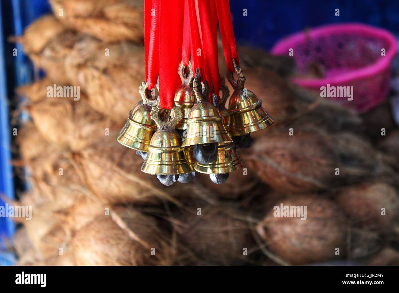 A collection of small brass temple bells on a red ribbon with cocoanuts ...