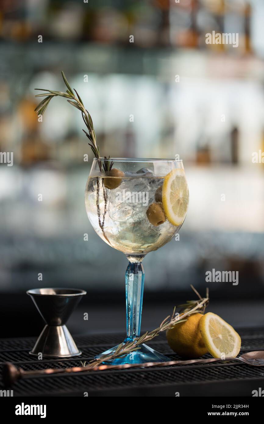 A vertical shot of a refreshing drink with lemon and olives on the bar ...