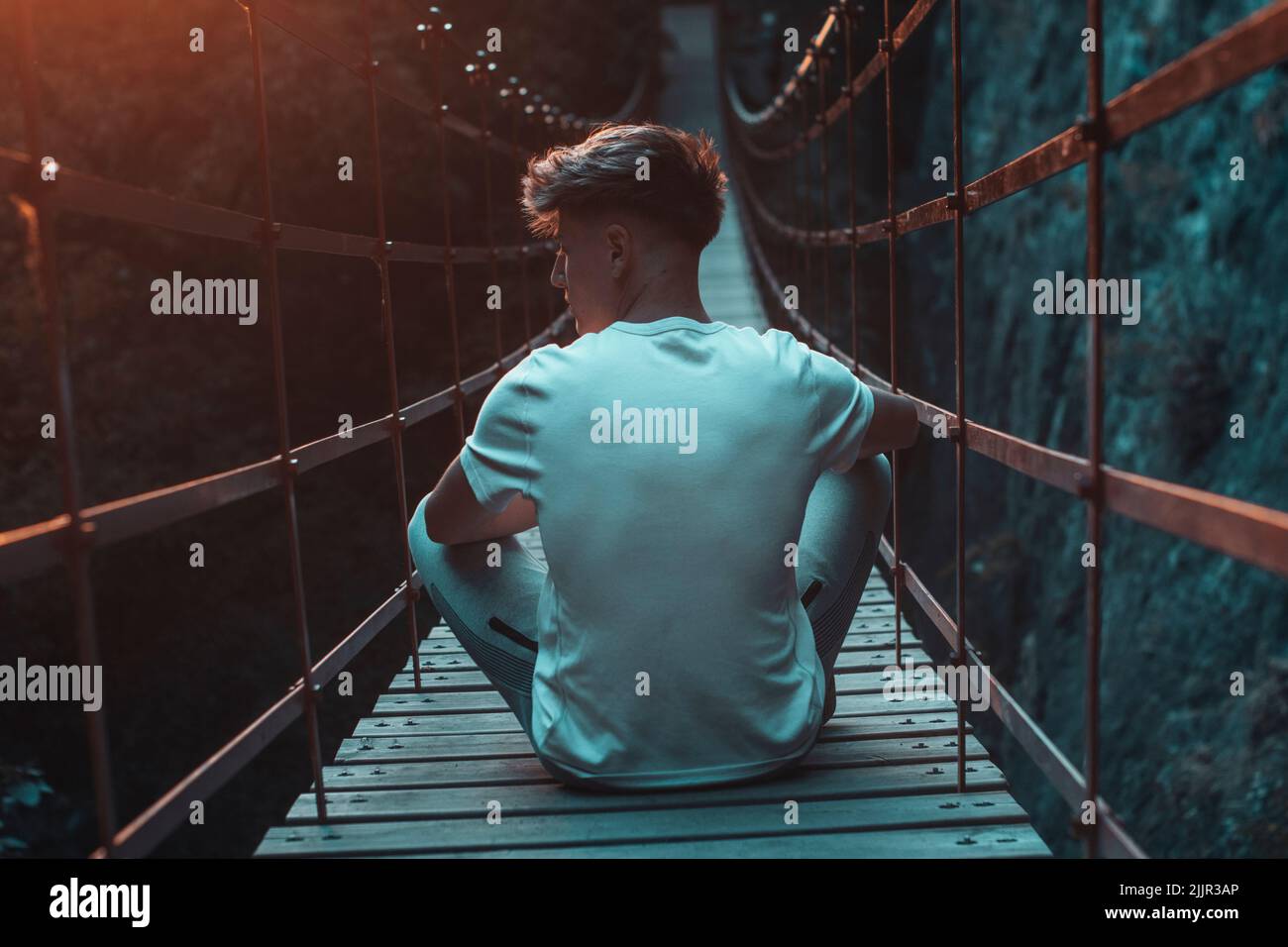 A caucasian boy sitting on a simple suspension bridge Stock Photo - Alamy