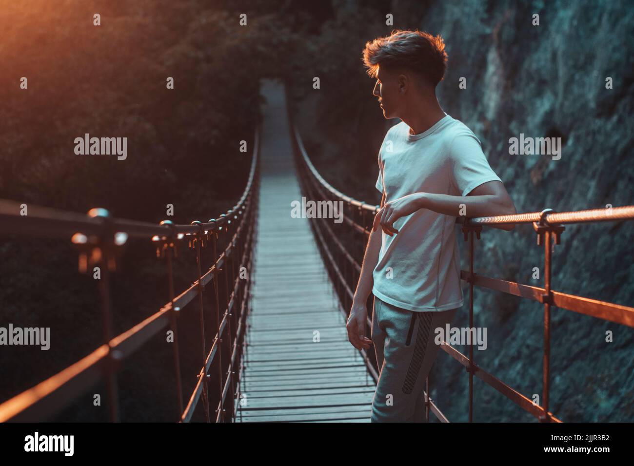 A pretty caucasian boy posing for a photo on a simple suspension bridge ...
