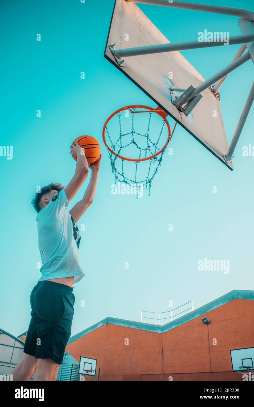 A vertical of a young male jumping and dunking a basketball into the ...