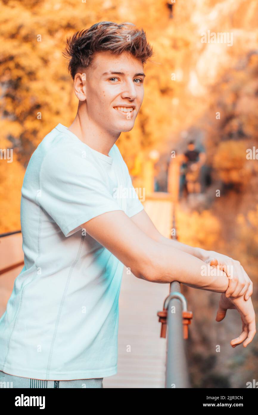 A Caucasian man leaning on the railing of the bridge in the fall park ...