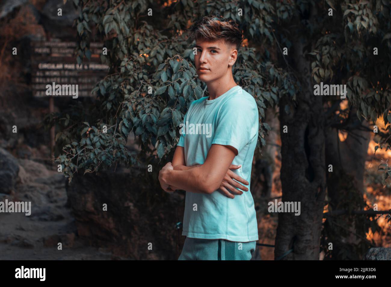 A young blonde Spanish man standing in the park with crossed hands ...