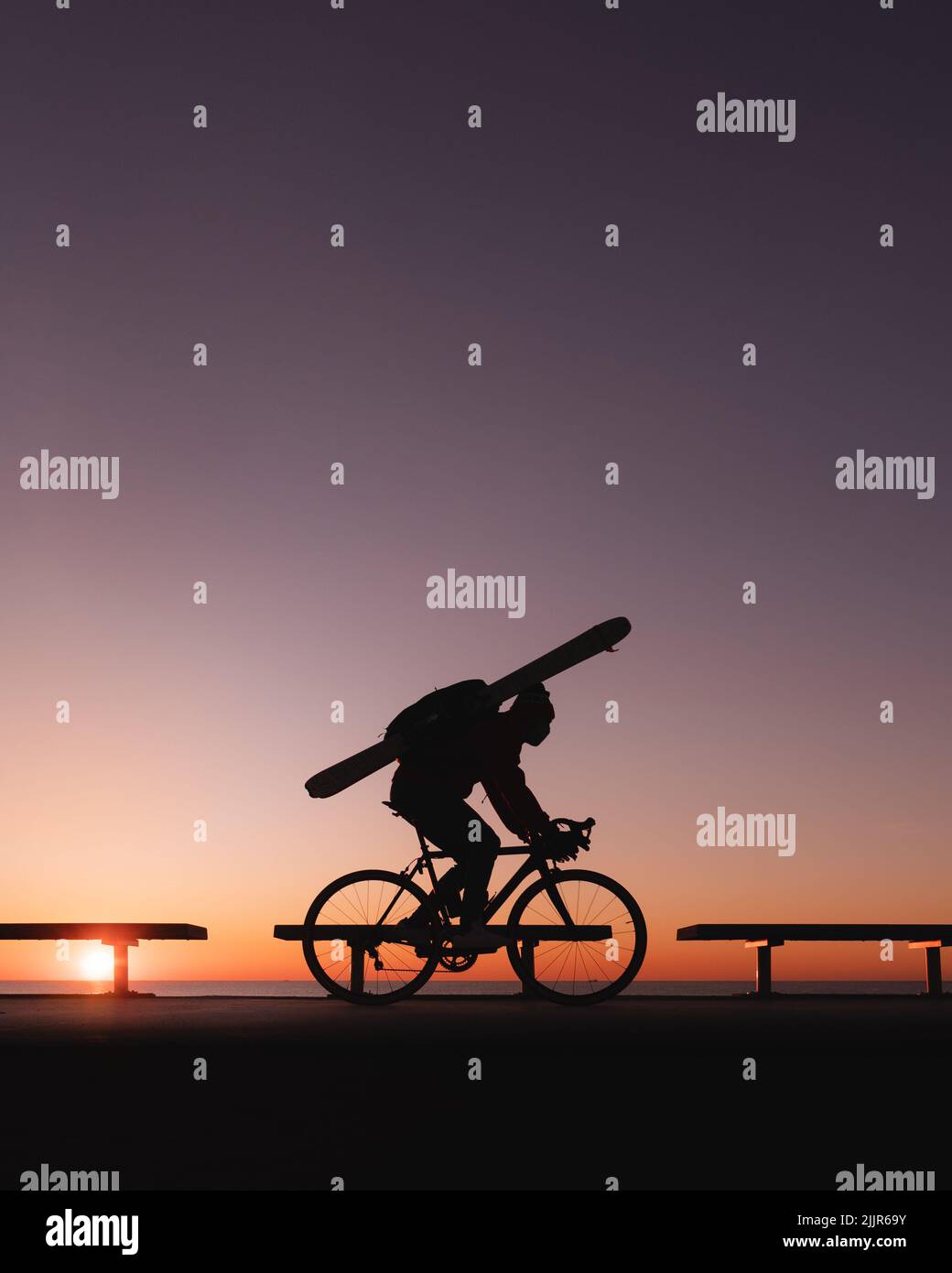 A vertical silhouette of a person riding a bicycle with the sunset sky ...