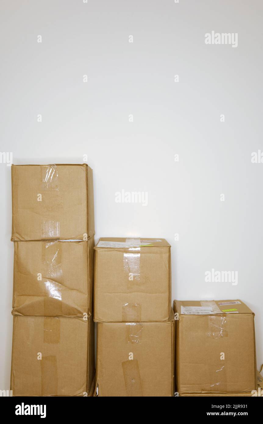 A vertical shot of boxes placed on each other in front of a white wall ...