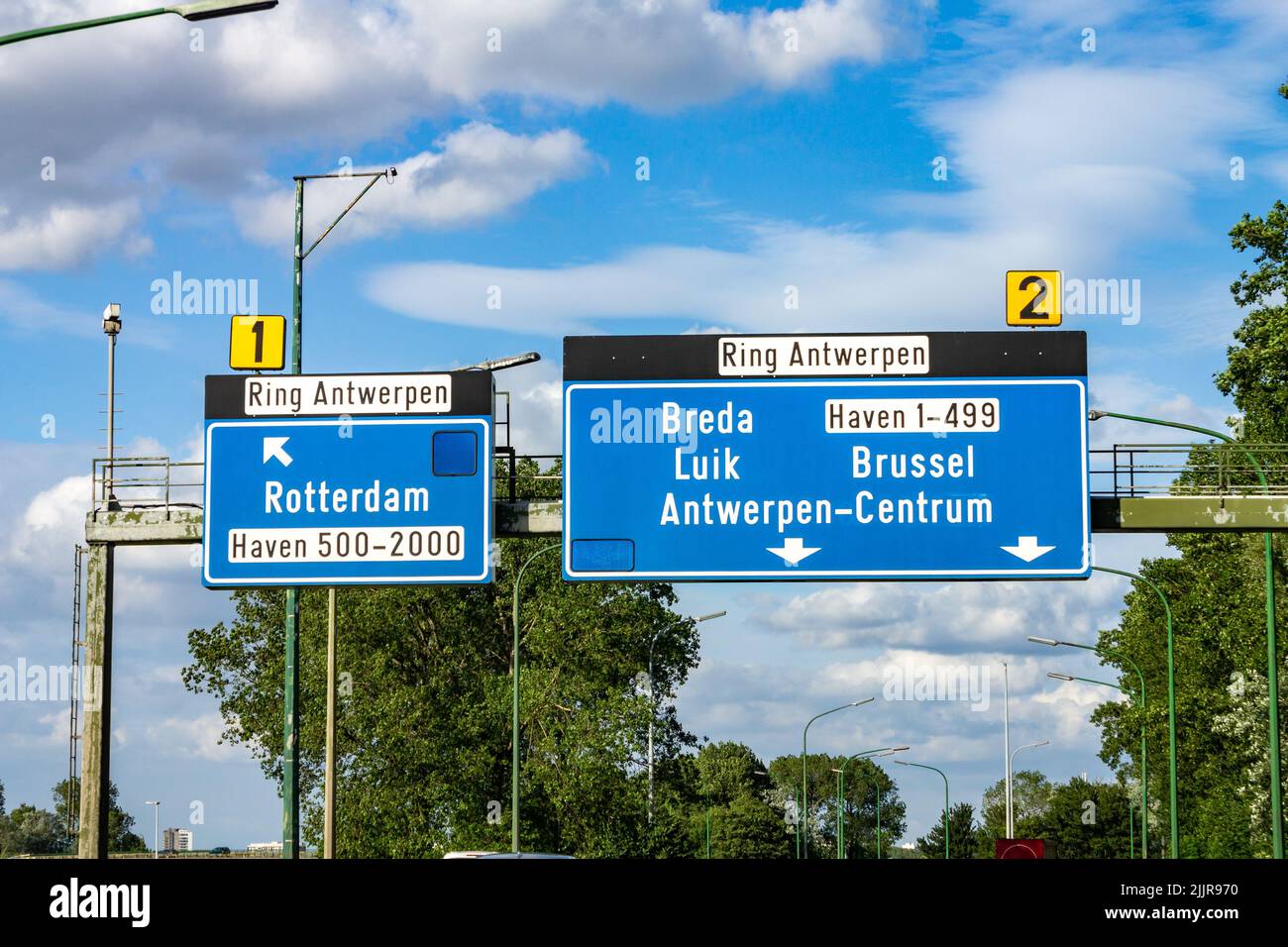A scenic view of road signs in Ghent, Belgium against green trees and a ...