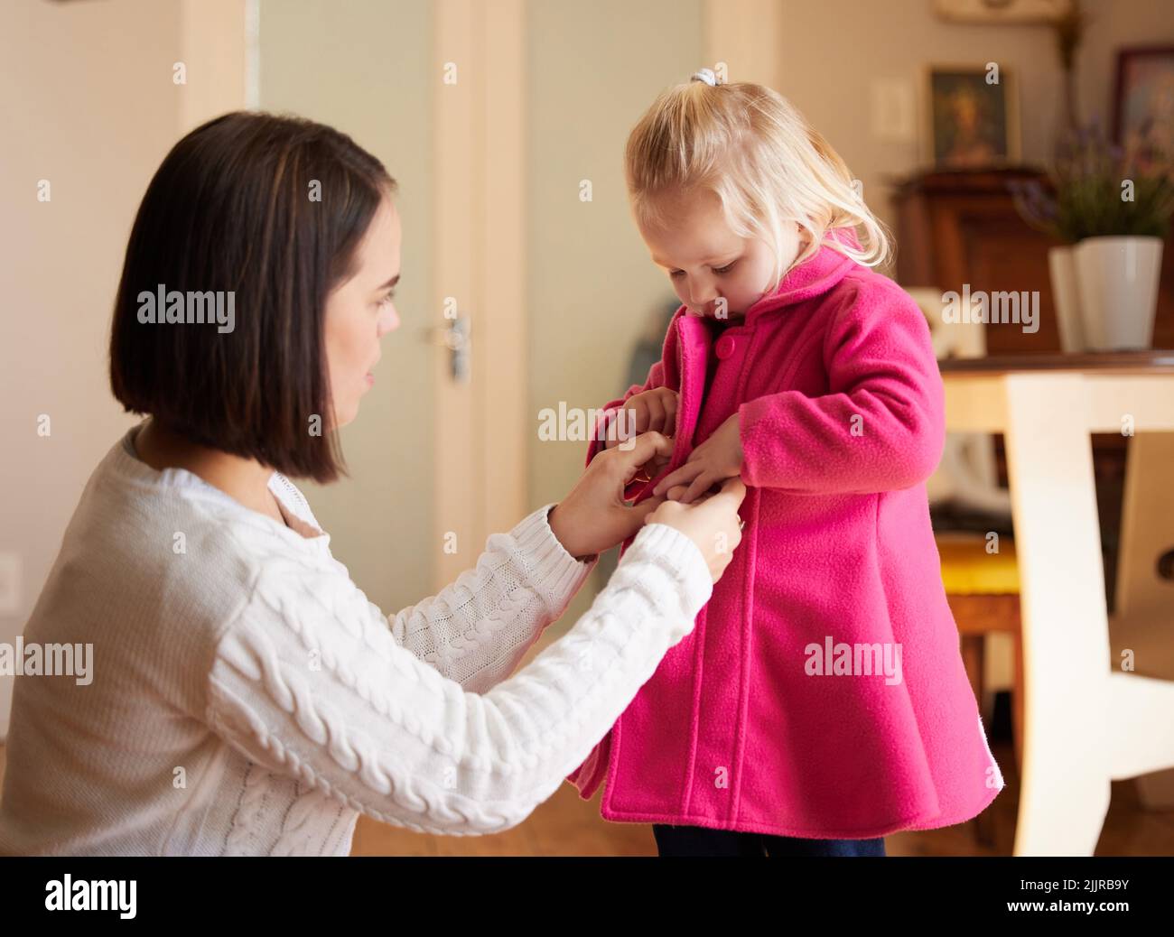 Baby its cold outside. a woman buttoning up her daughters pink coat ...