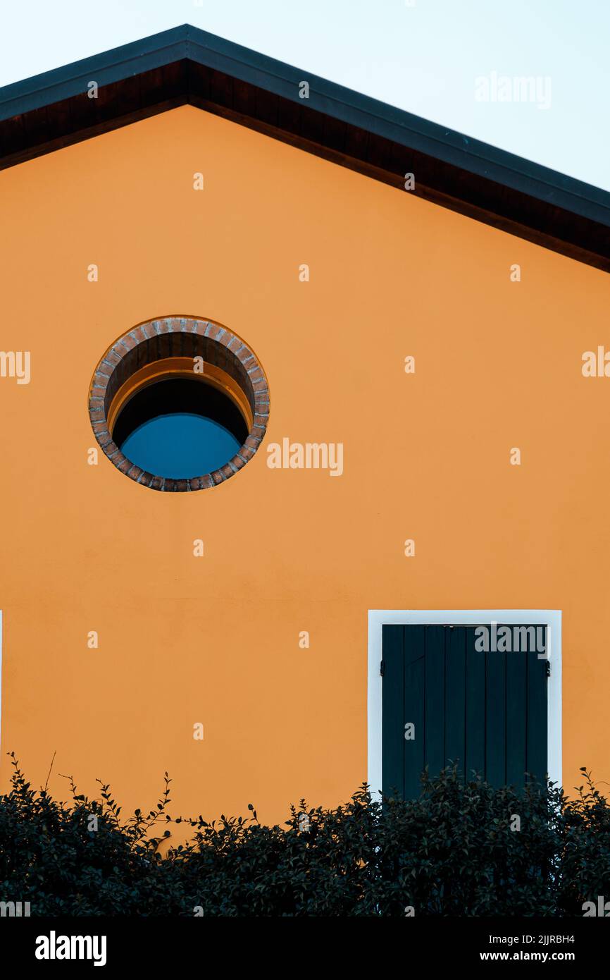A vertical shot of an orange facade of a building with a circle window ...